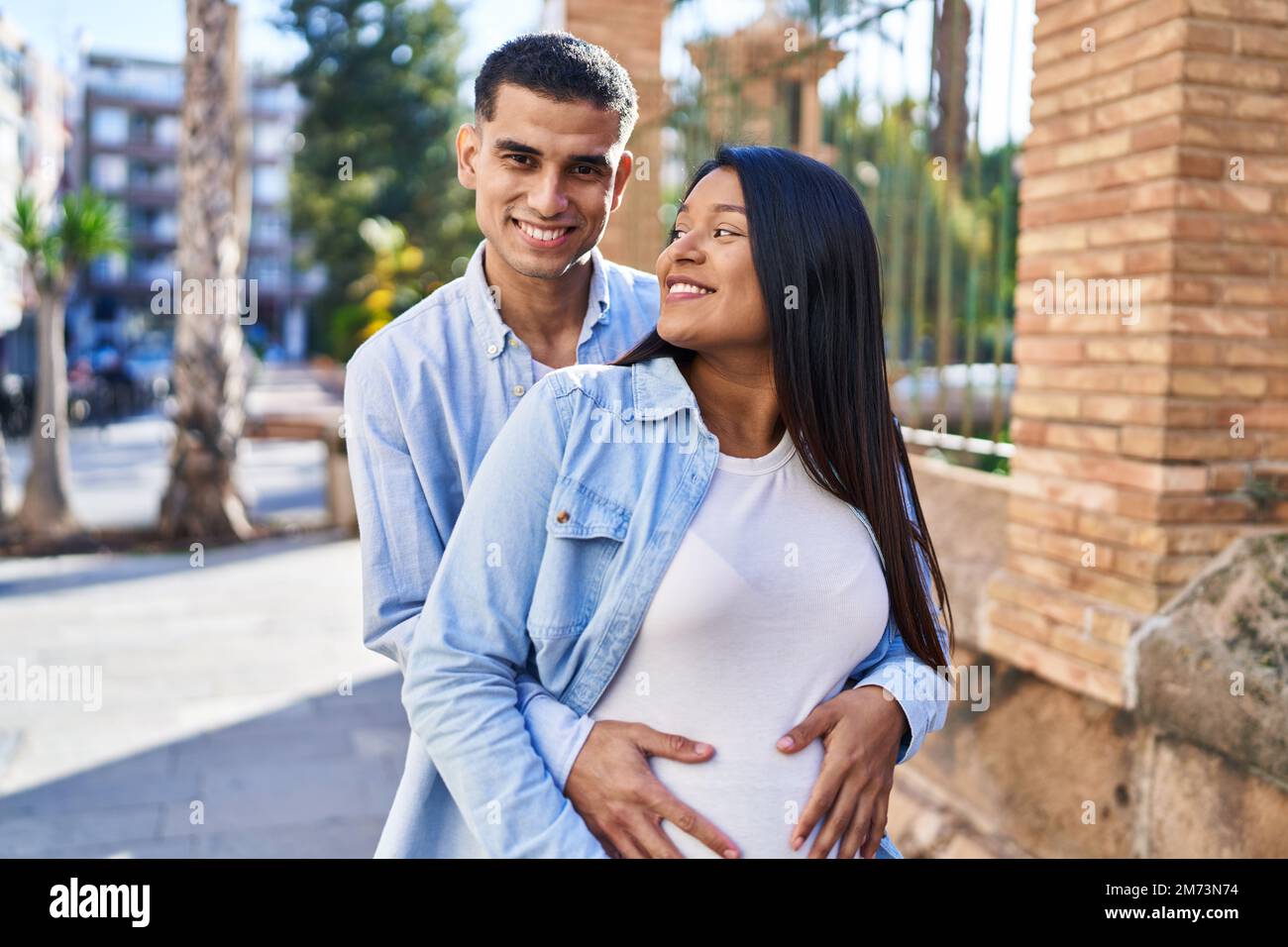 Young latin couple expecting baby hugging each other standing at street Stock Photo - Alamy