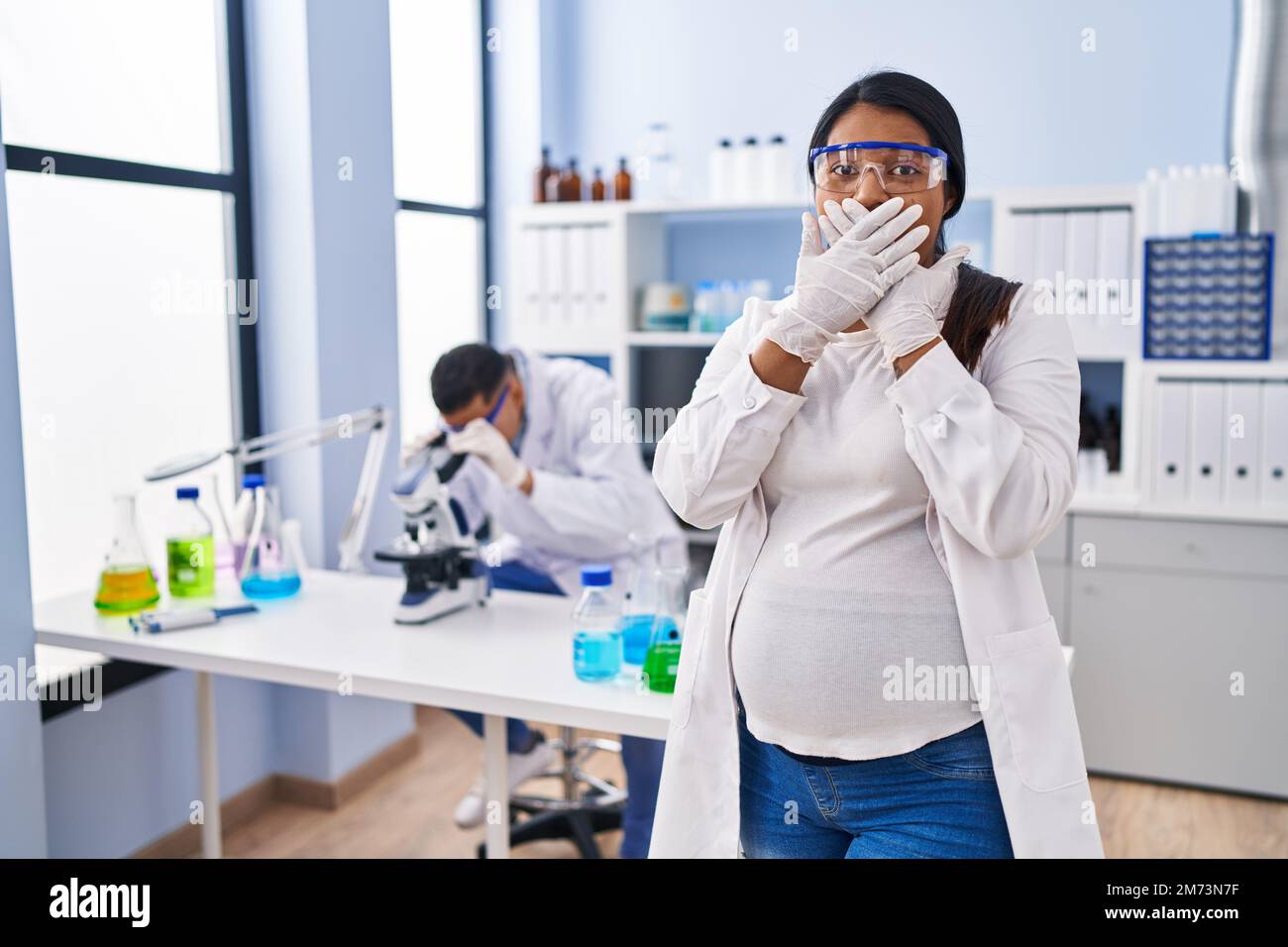 Young hispanic woman expecting a baby working at scientist laboratory ...