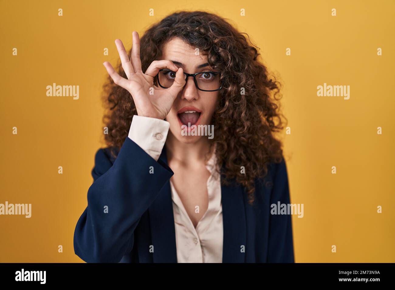 Hispanic woman with curly hair standing over yellow background doing ok ...