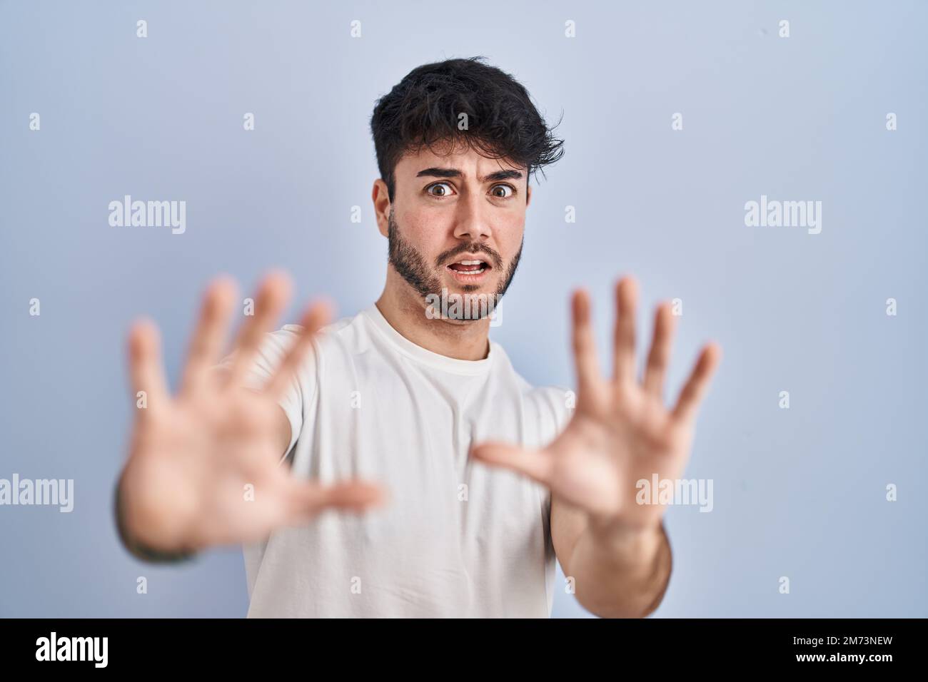 Hispanic man with beard standing over white background afraid and ...
