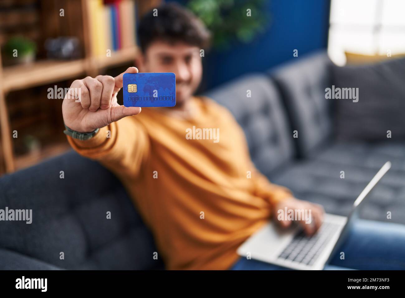 Young hispanic man using laptop and credit card sitting on sofa at home ...