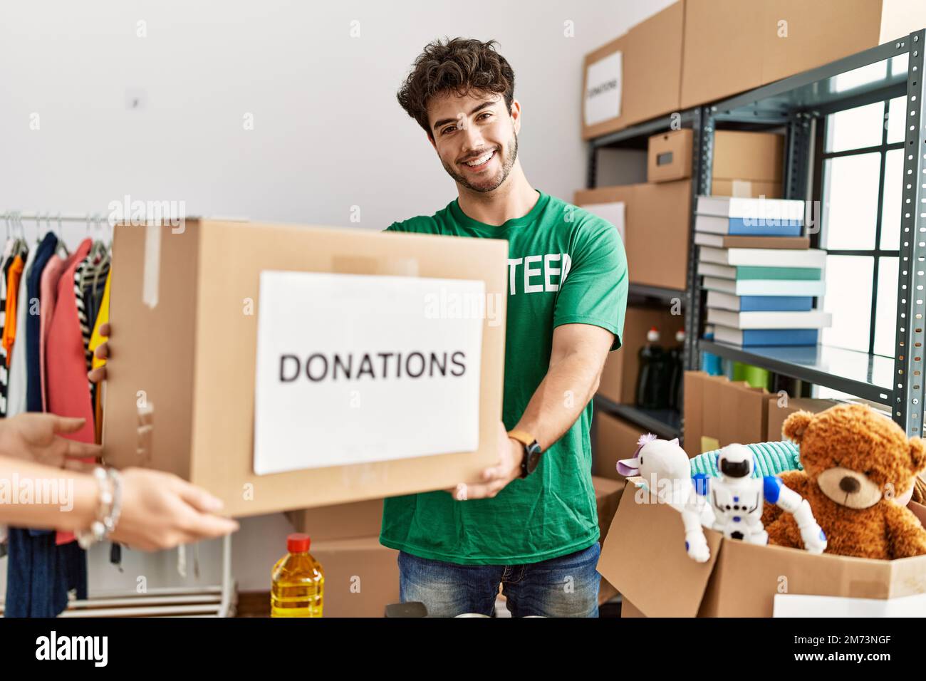 Young hispanic man wearing volunteer uniform giving donations box at ...
