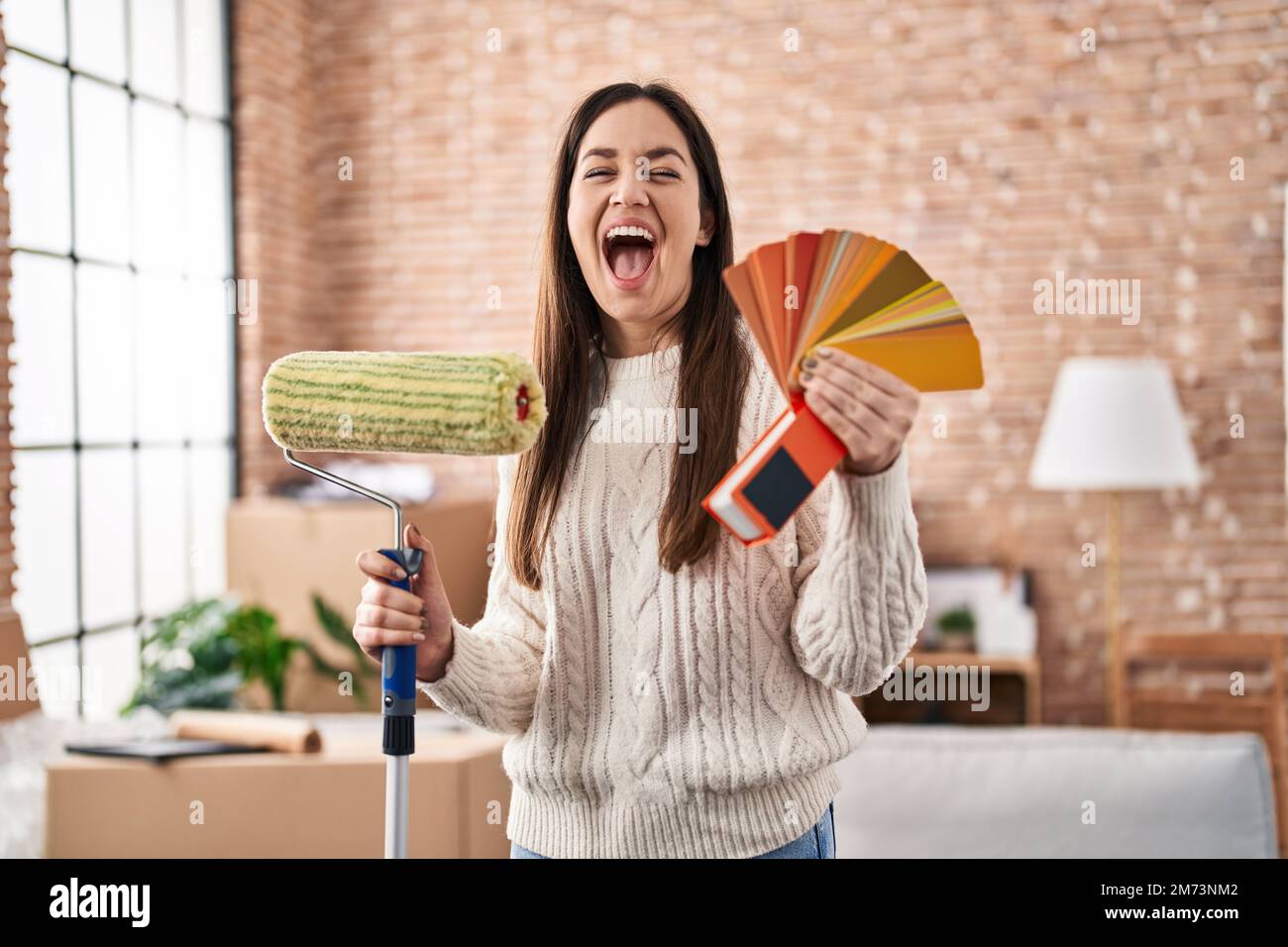 Young brunette woman holding roller painter and paint samples ...