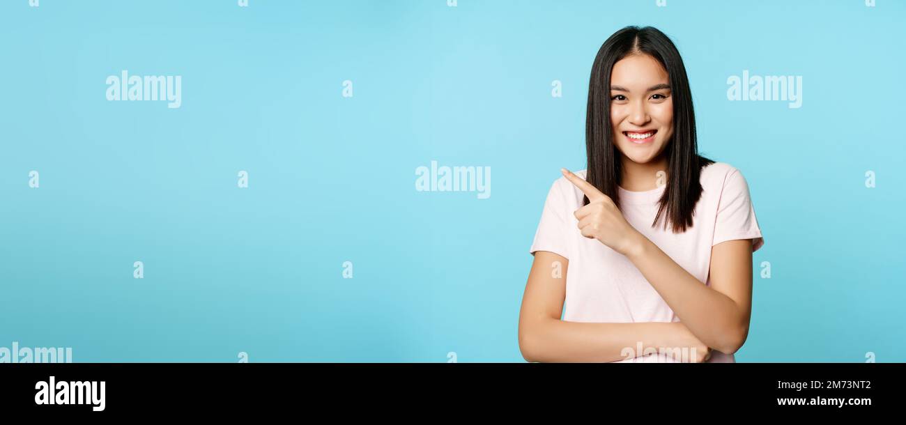 Portrait of happy smiling asian female model, pointing at upper left ...