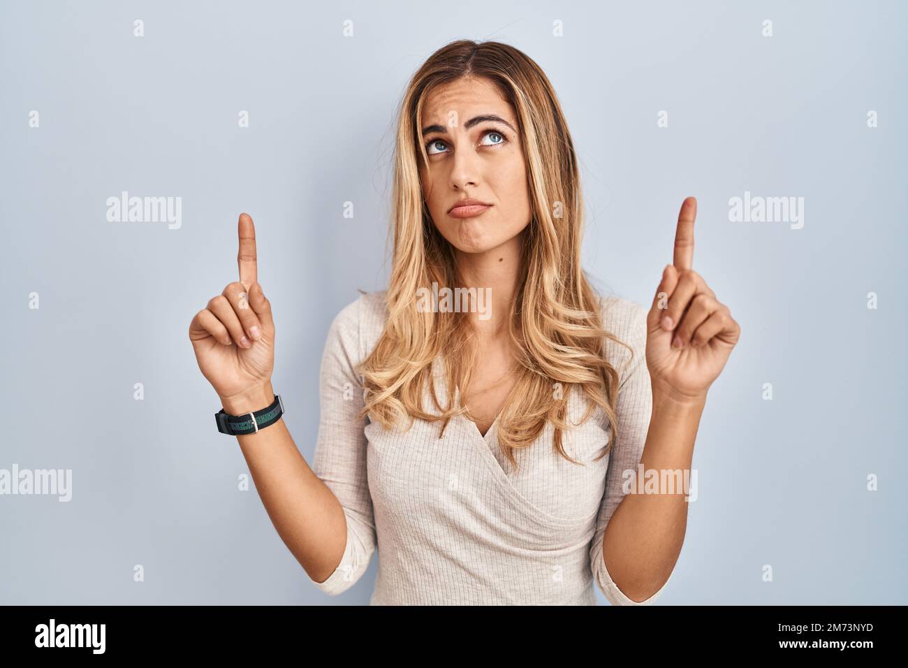 Young blonde woman standing over isolated background pointing up ...