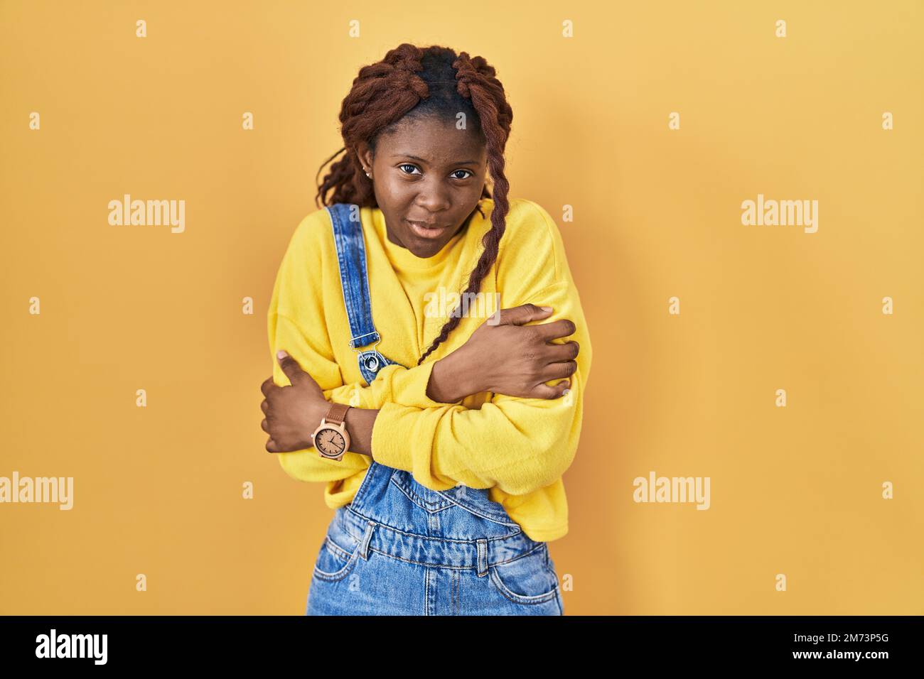 African woman standing over yellow background shaking and freezing for ...