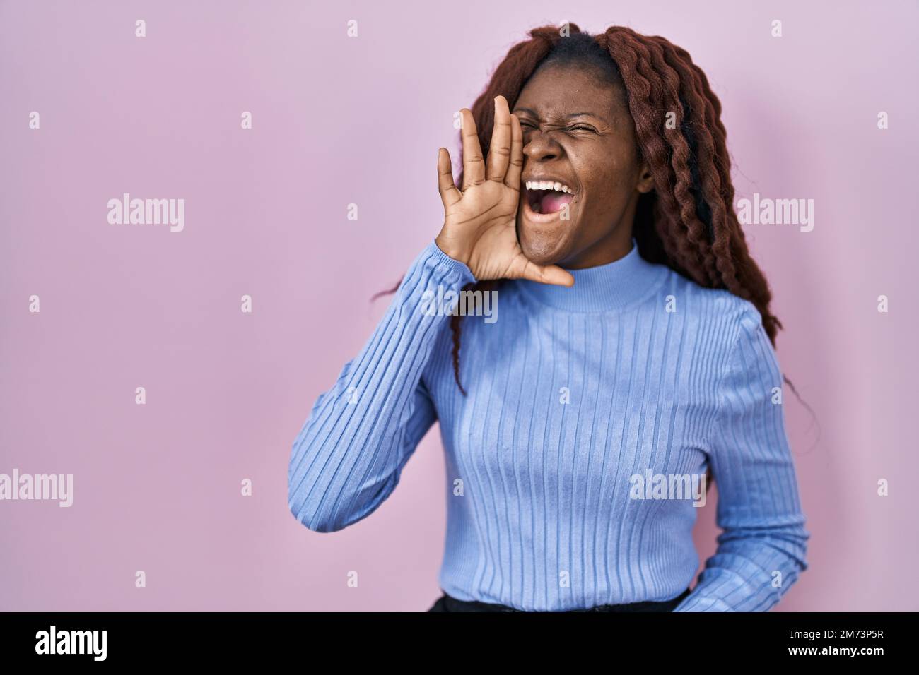 African woman standing over pink background shouting and screaming loud ...