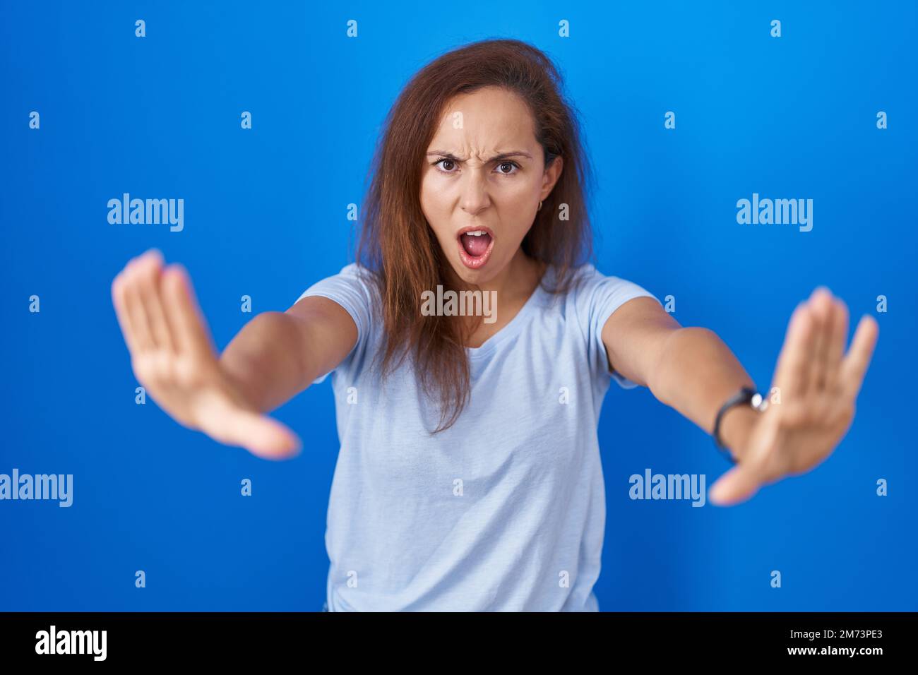 Brunette woman standing over blue background doing stop gesture with ...