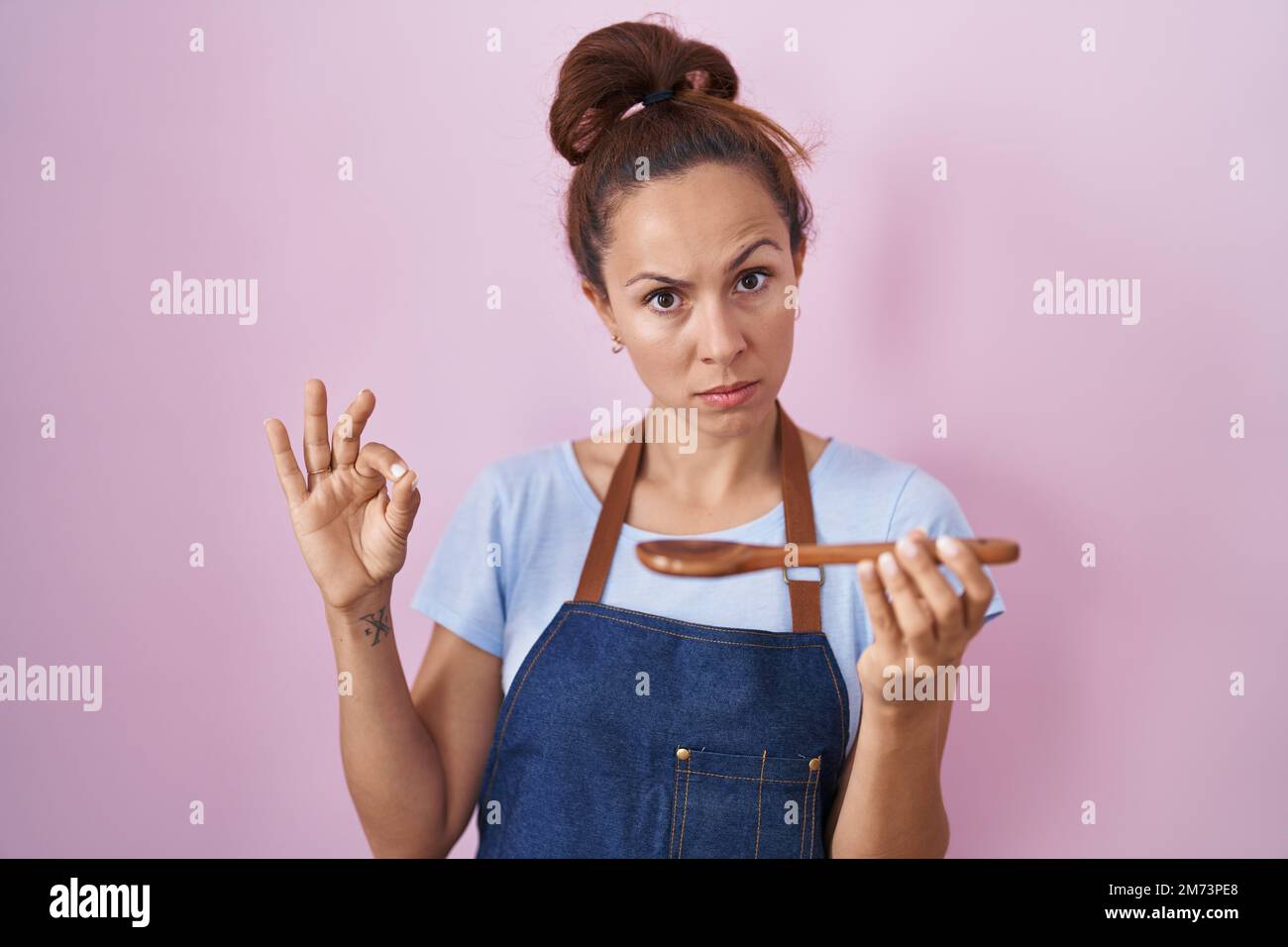 Brunette woman wearing professional cook apron holding wooden spoon ...