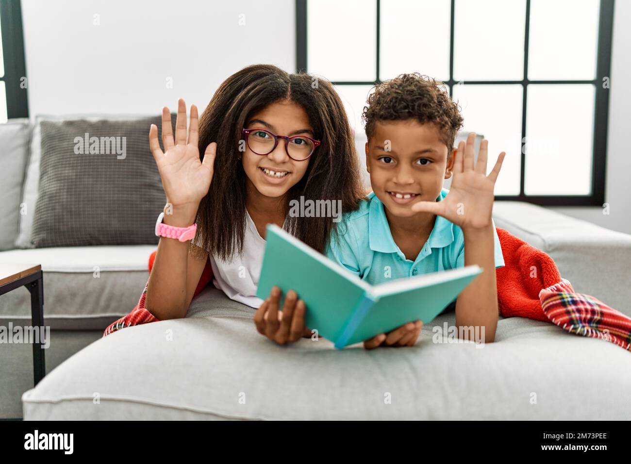 Two siblings lying on the sofa reading a book waiving saying hello ...