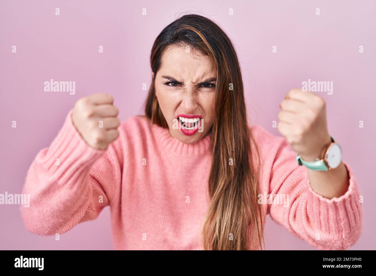 Young hispanic woman standing over pink background angry and mad ...
