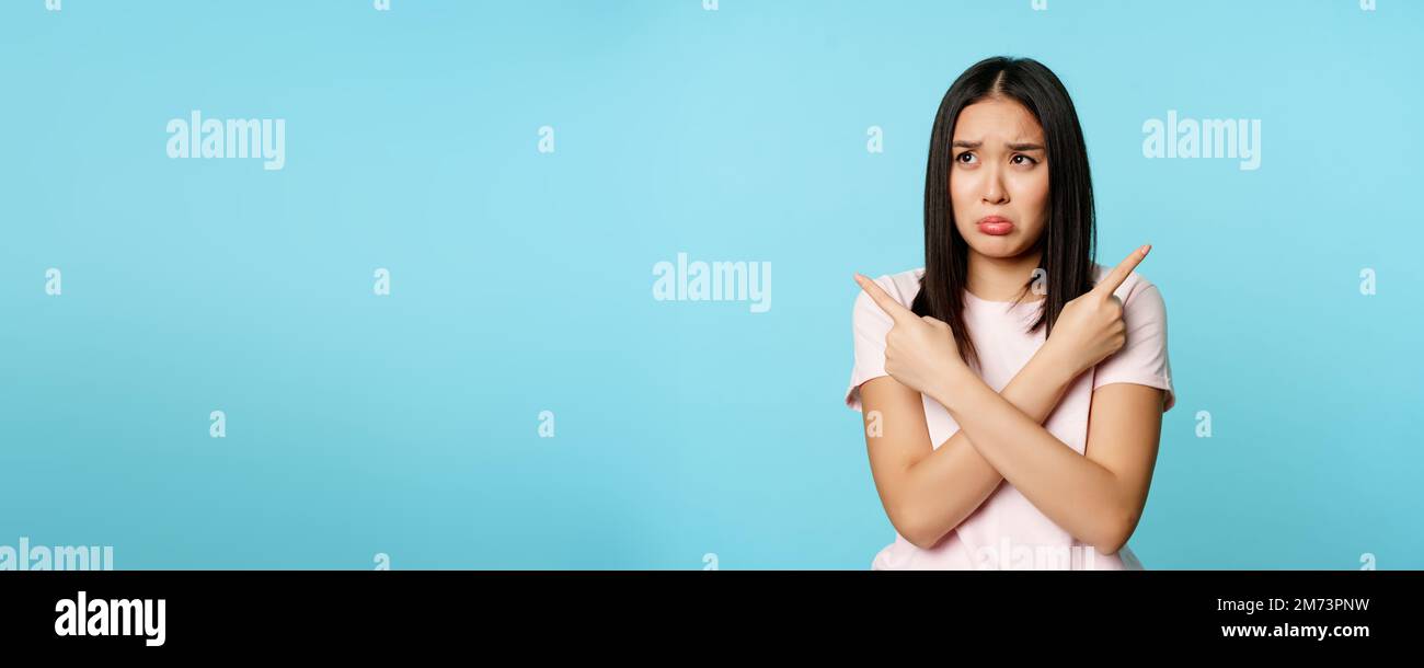 Confused and sad asian girl pointing sideways, looking clueless or ...