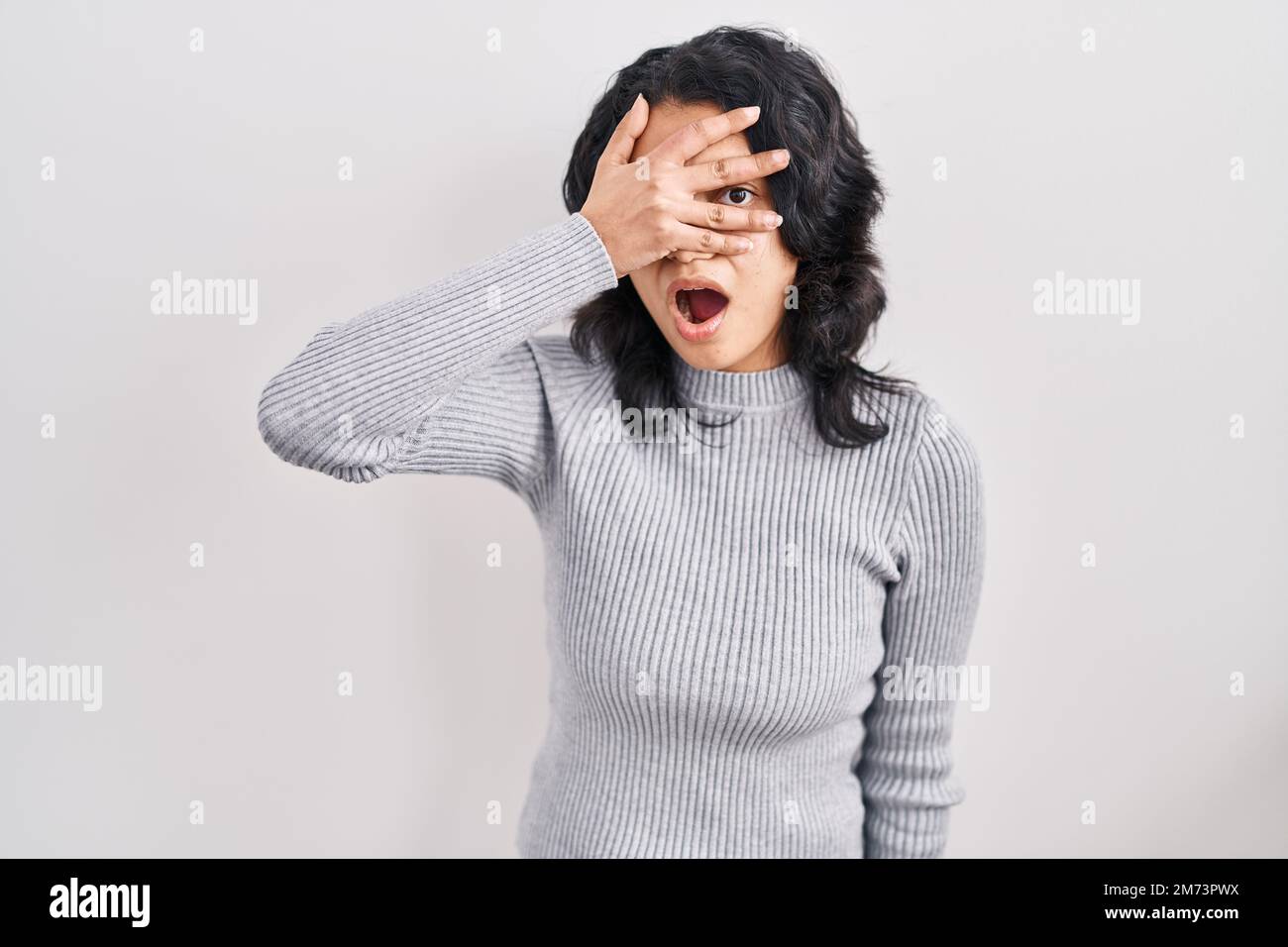 Hispanic woman with dark hair standing over isolated background peeking ...