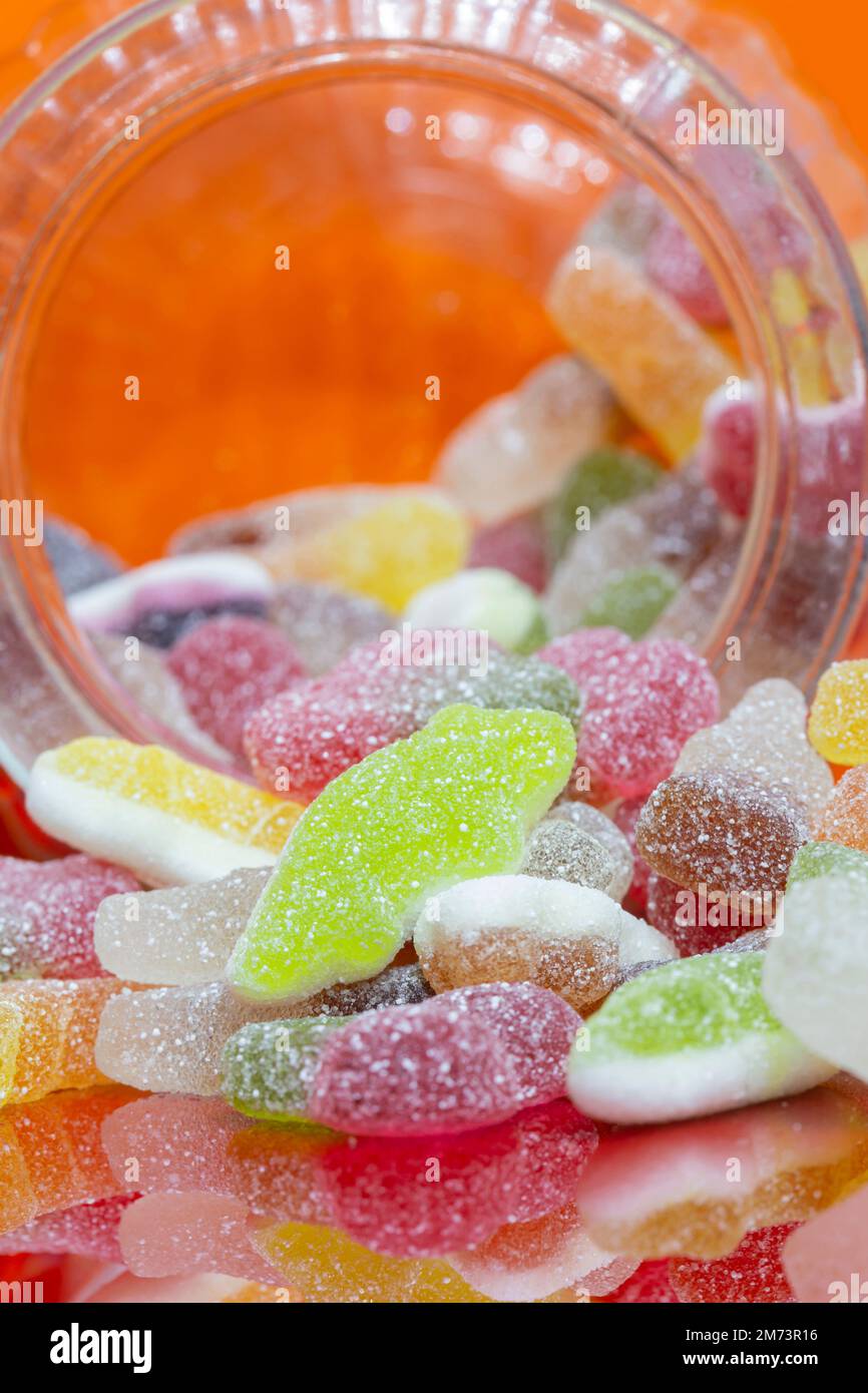 Mixture of sugar coated sweets candy in a glass jar. On an orange ...