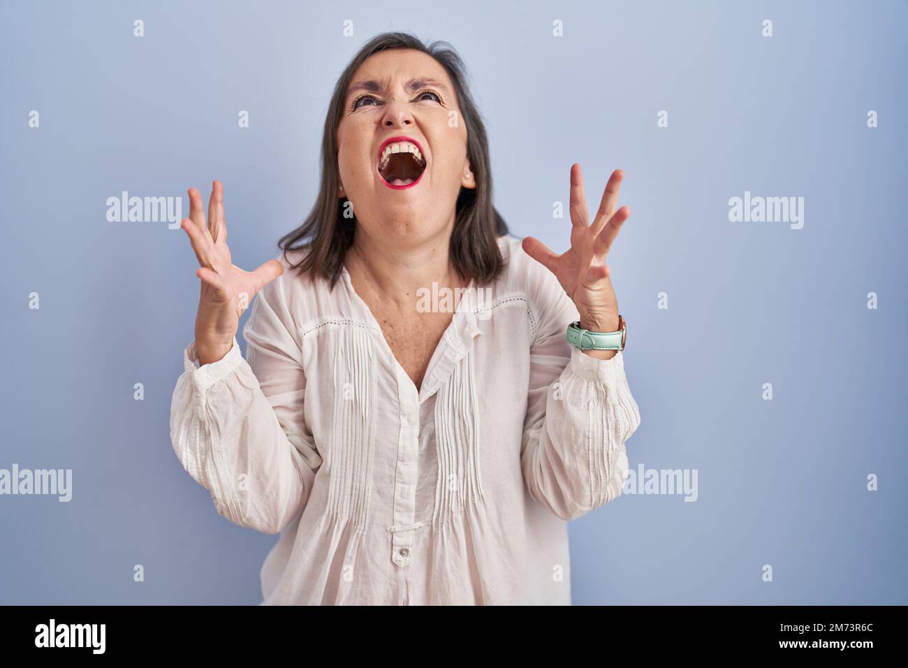 Middle age hispanic woman standing over blue background crazy and mad ...