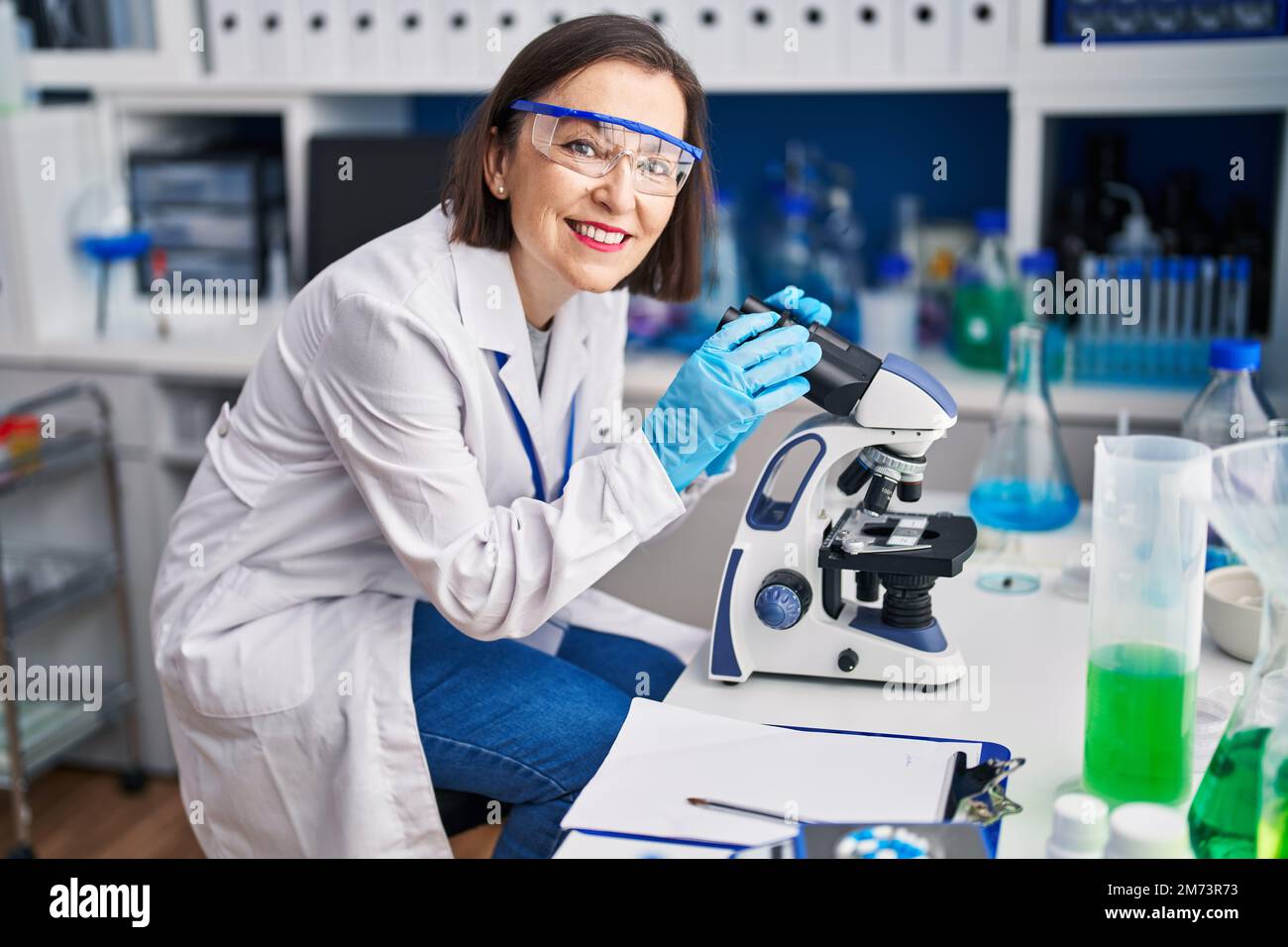 Middle age woman scientist smiling confident using microscope at ...