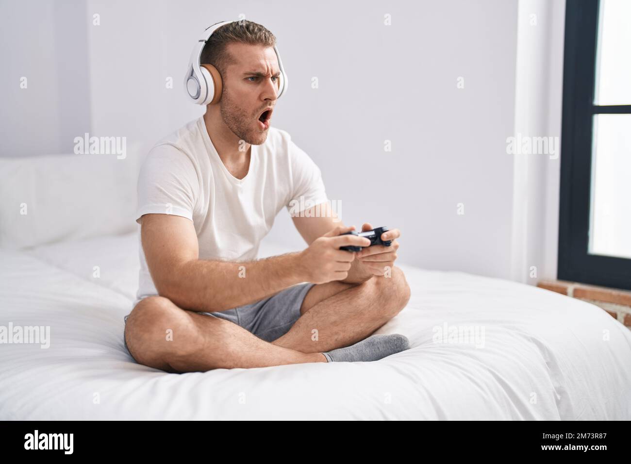 Young caucasian man sitting on the bed at home playing video games in ...