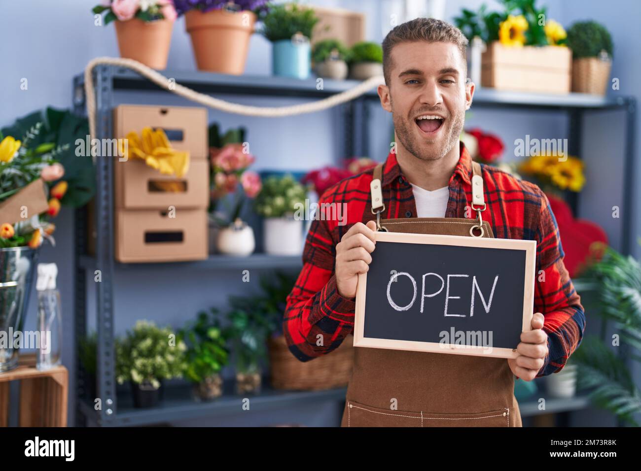 Young caucasian man working at florist holding open sign smiling and ...