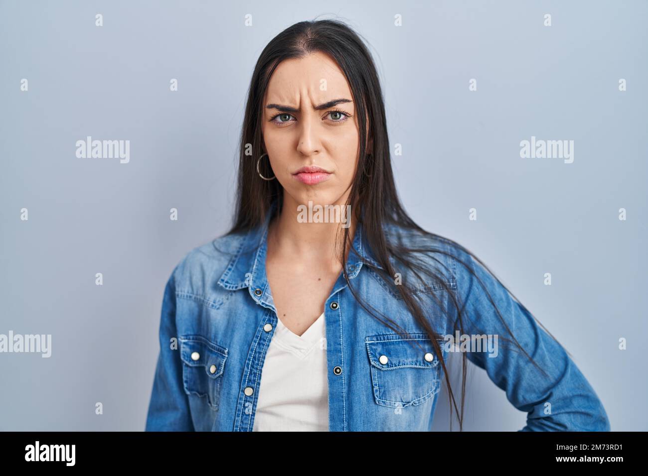 Hispanic woman standing over blue background skeptic and nervous ...