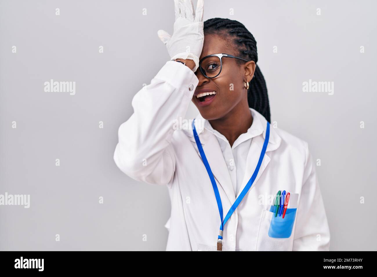 African woman with braids wearing scientist uniform surprised with hand ...