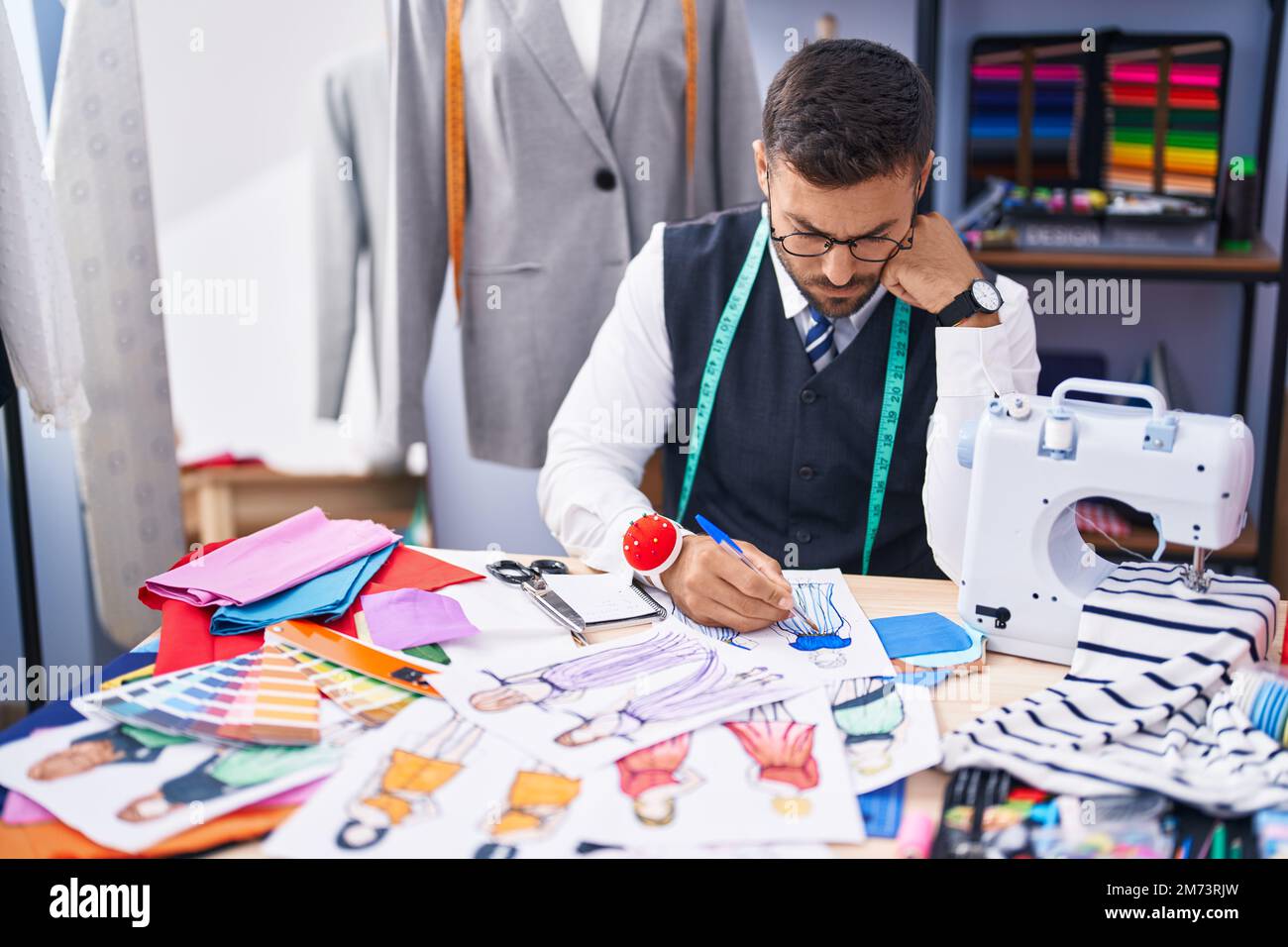 Young hispanic man tailor drawing clothing design on notebook at tailor ...