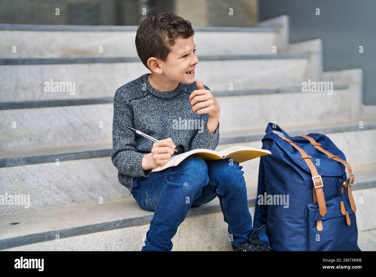 Blond child student writing on book sitting on stairs at school Stock ...