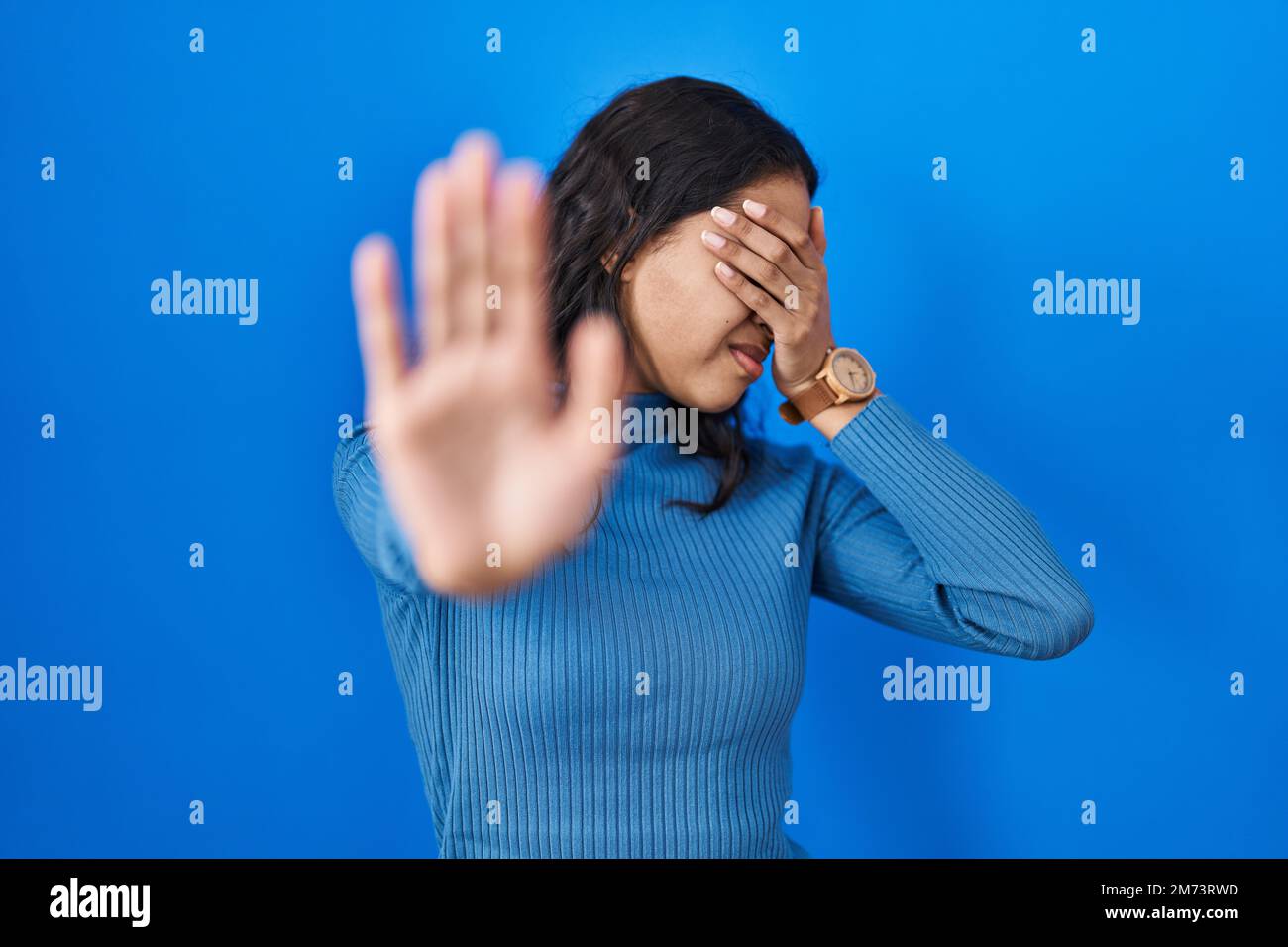 Young brazilian woman standing over blue isolated background covering ...