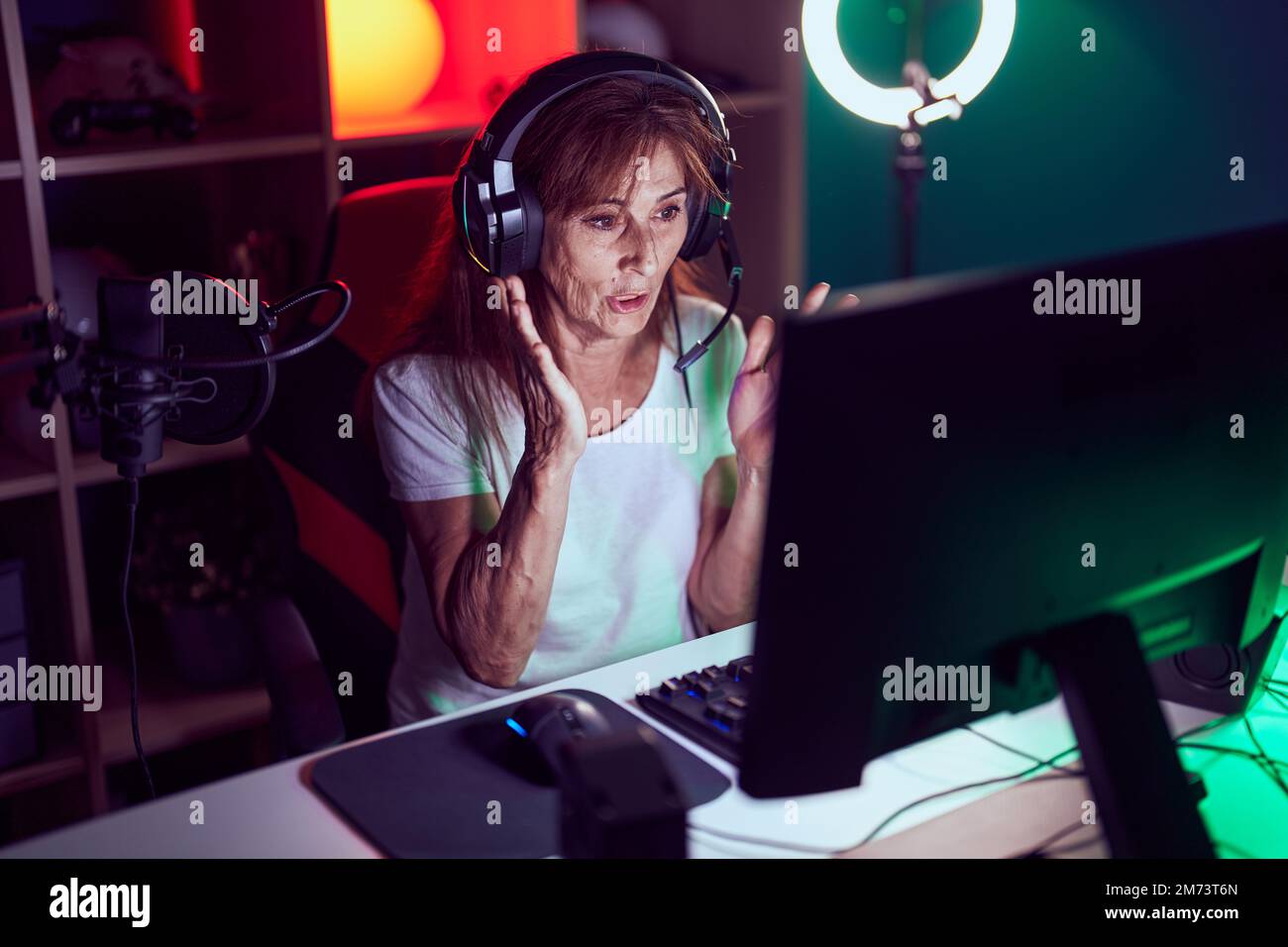 Middle age woman streamer playing video game using computer at gaming ...