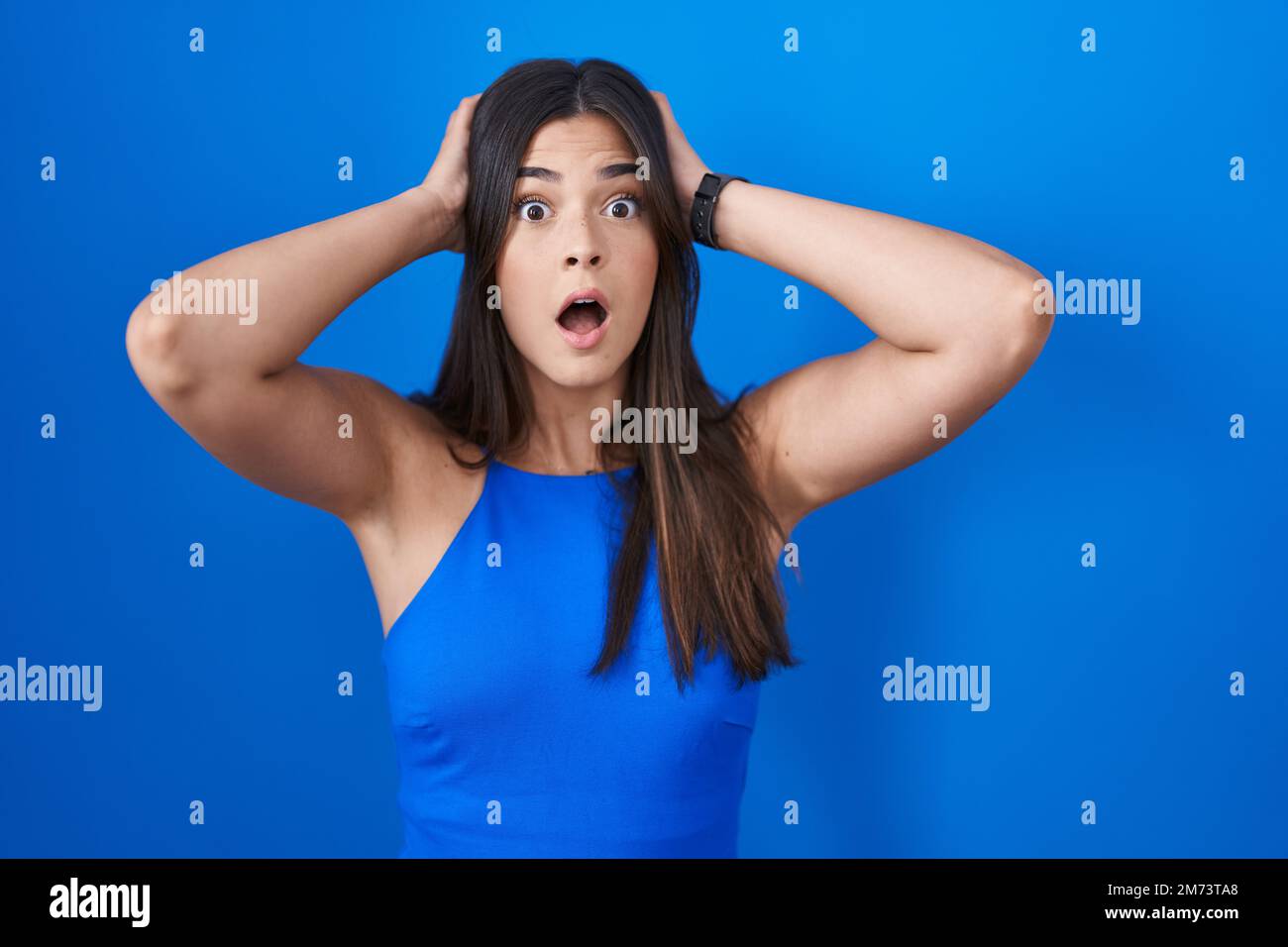Hispanic woman standing over blue background crazy and scared with ...