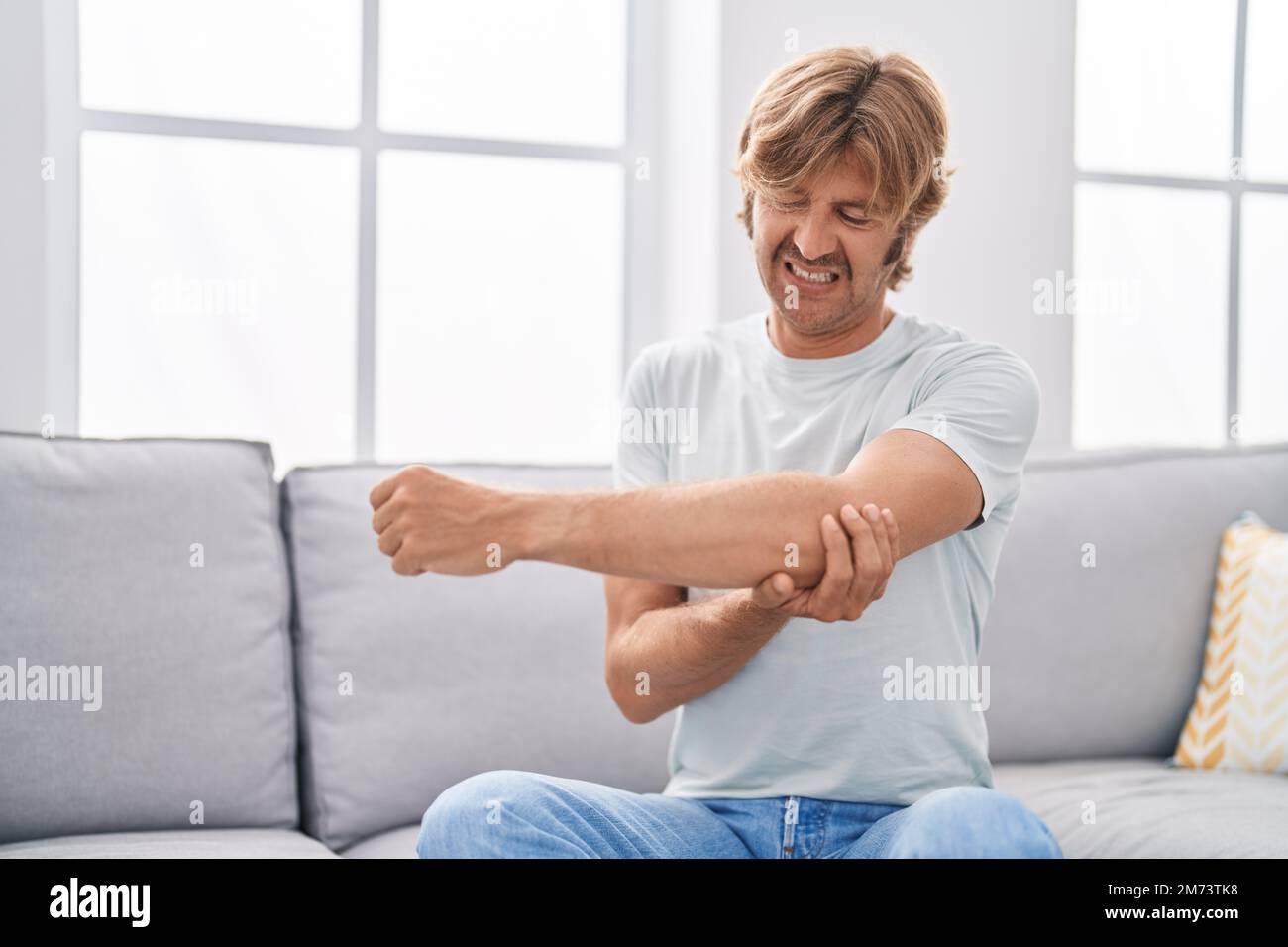 Young man suffering for elbow pain sitting on sofa at home Stock Photo ...