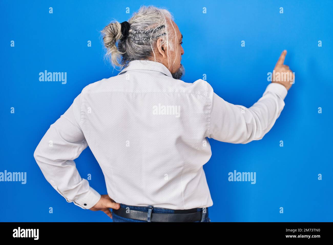 Middle age man with grey hair standing over blue background posing ...