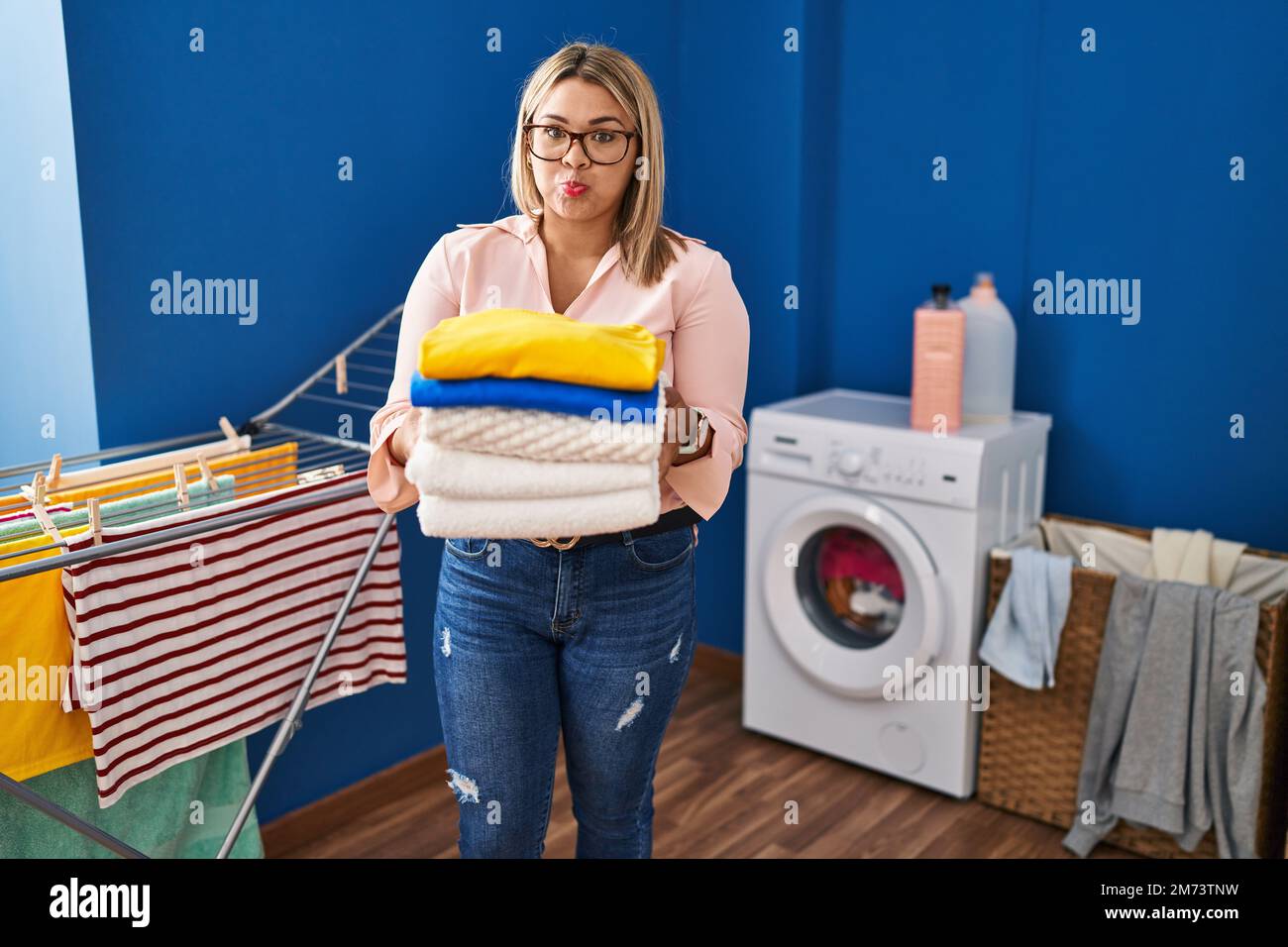 Young hispanic woman holding folded laundry after ironing puffing ...