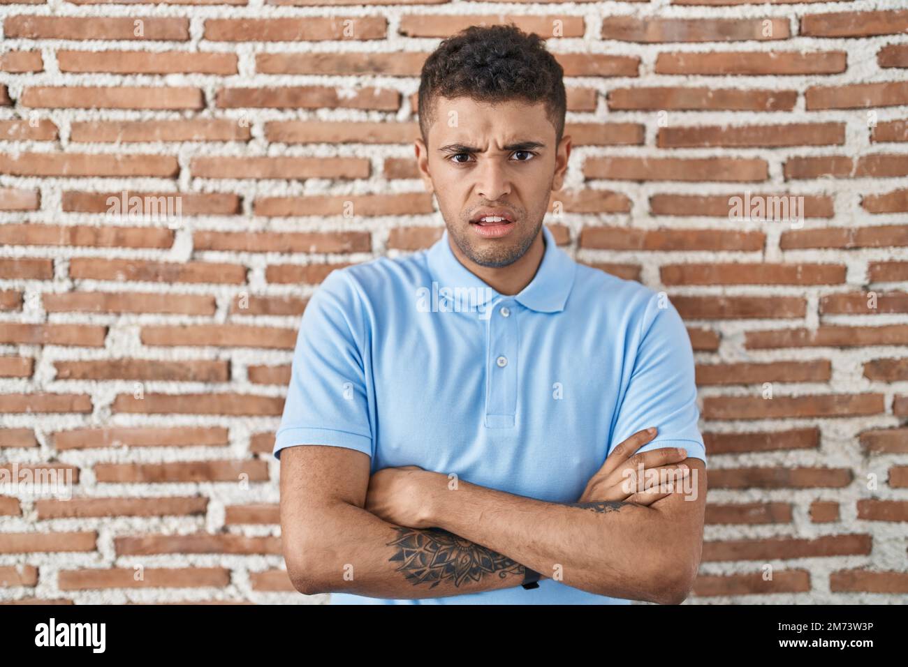 Brazilian young man standing over brick wall skeptic and nervous ...