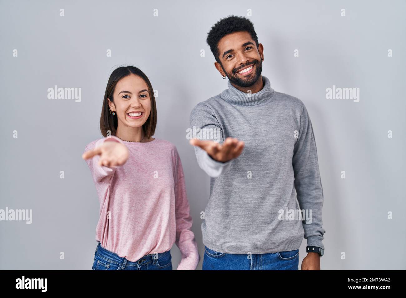 Young hispanic couple standing together smiling cheerful offering palm ...