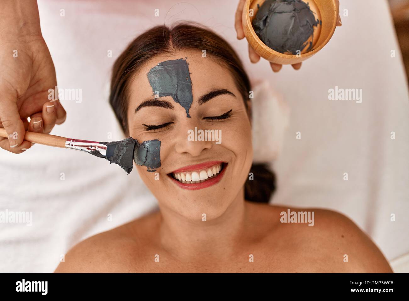 Young beautiful hispanic woman lying on table having facial treatment ...