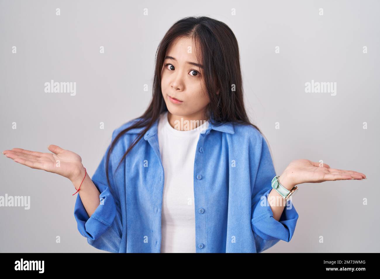 Young chinese woman standing over white background clueless and ...