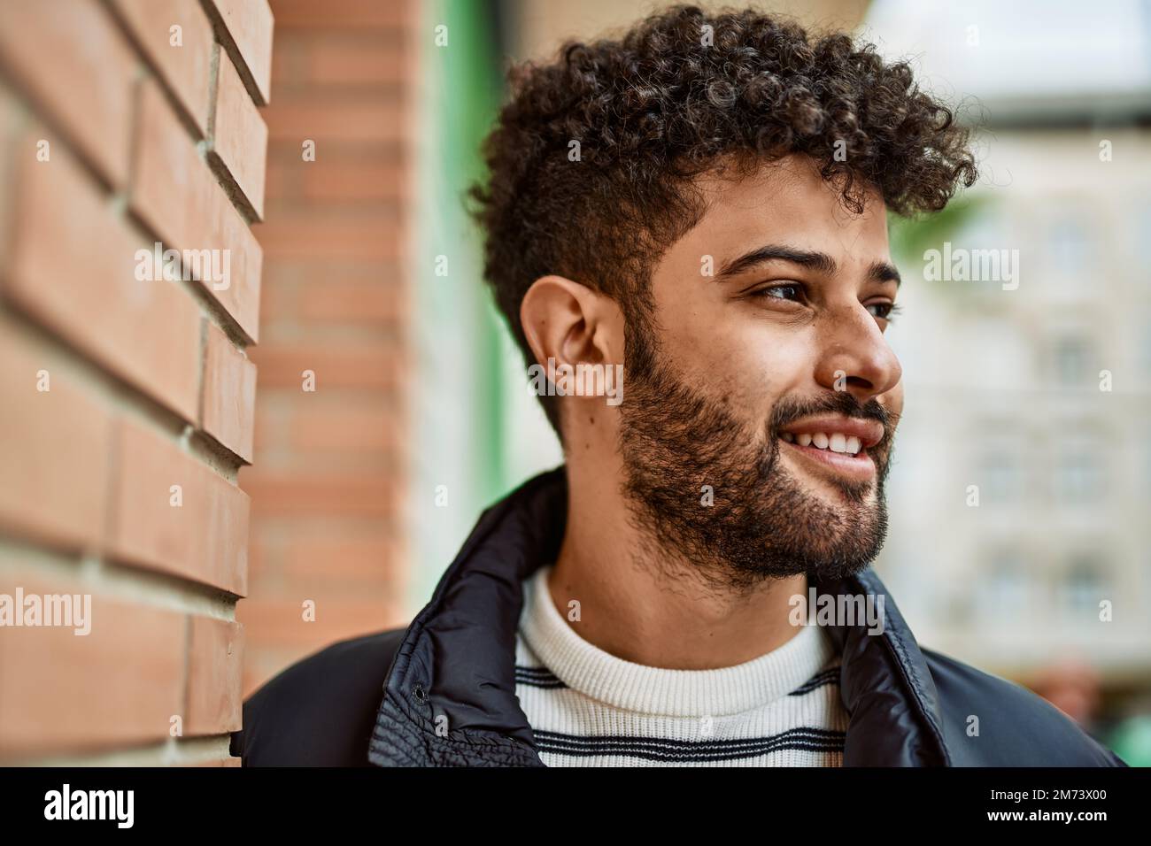 Young arab man smiling leaning on bricks wall Stock Photo - Alamy
