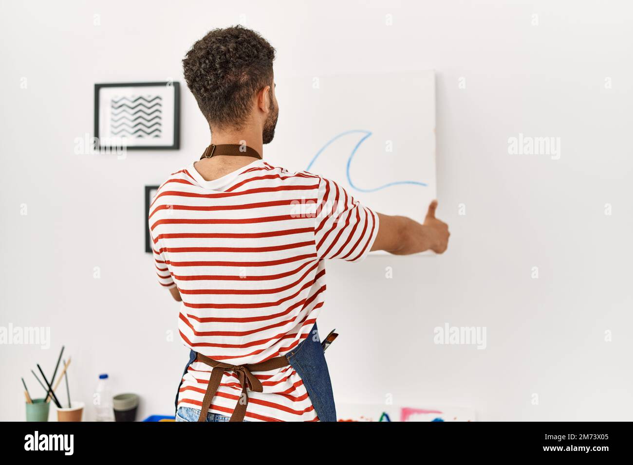 Young arab artist man on back view hanging draw canvas on wall at art ...