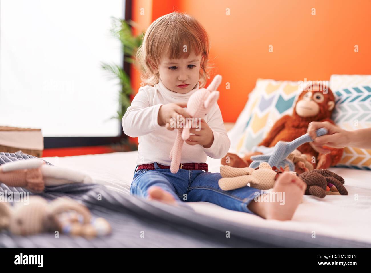 Adorable hispanic girl holding dolls sitting on bed at bedroom Stock ...
