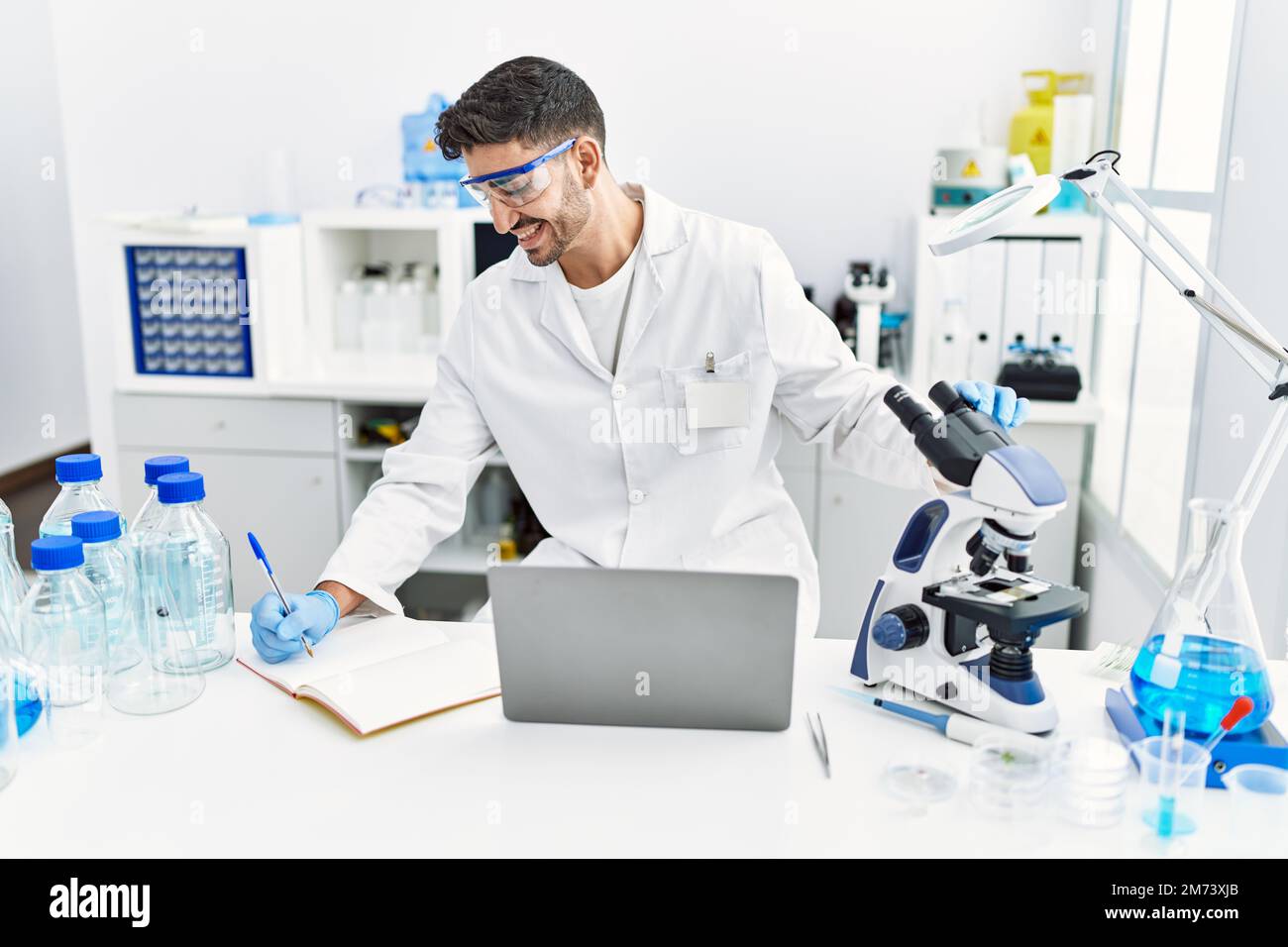 Handsome hispanic man working as scientific with microscope and laptop ...