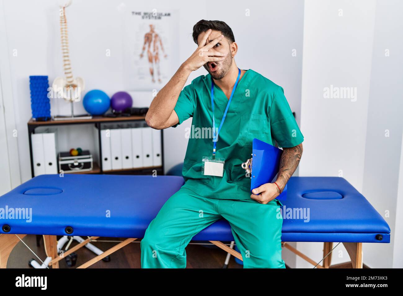 Young physiotherapist man working at pain recovery clinic peeking in ...