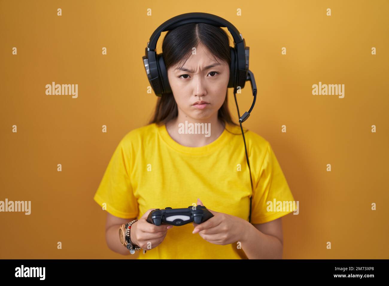 Chinese young woman playing video game holding controller depressed and ...