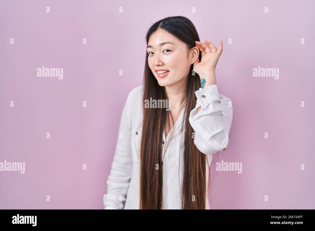 Chinese young woman standing over pink background smiling with hand ...