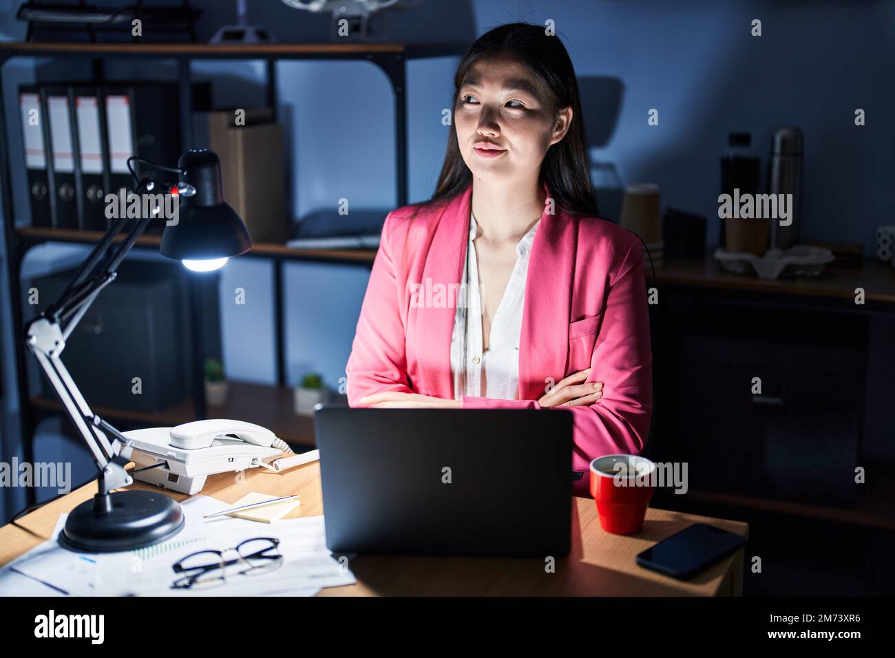 Chinese young woman working at the office at night smiling looking to ...