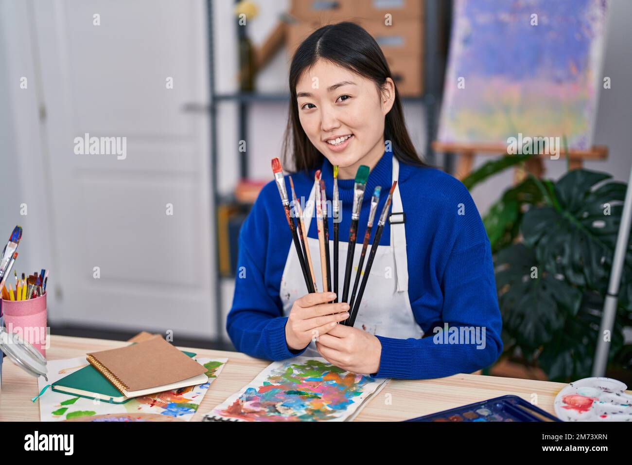 Chinese woman artist holding paintbrushes sitting on table at art ...