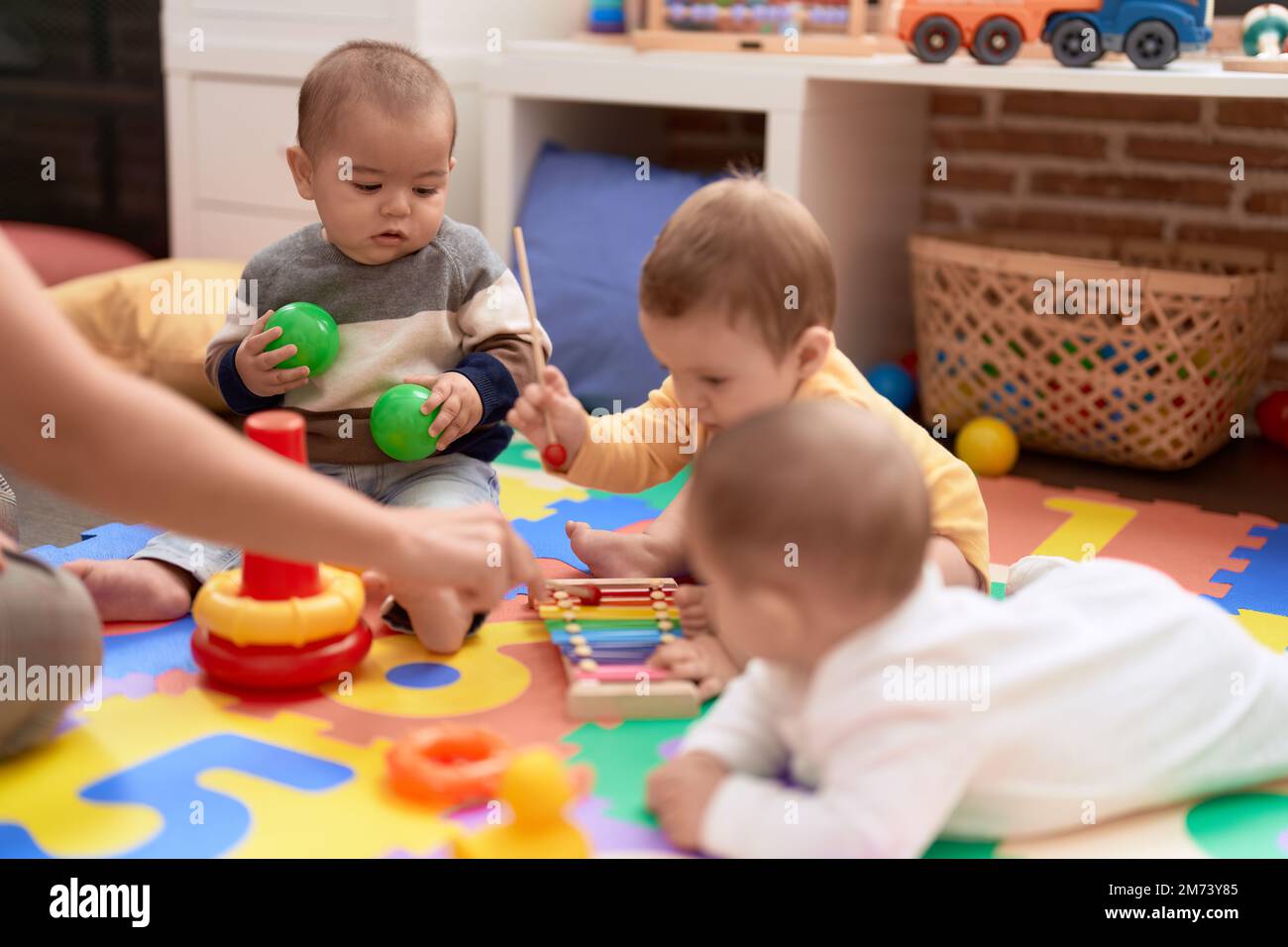 Group of toddlers playing with toys sitting on floor at kindergarten ...