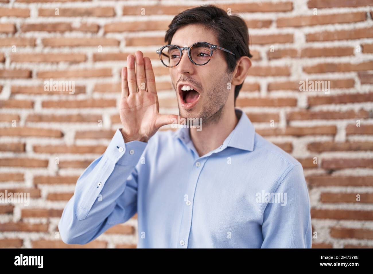 Young hispanic man standing over brick wall background shouting and ...