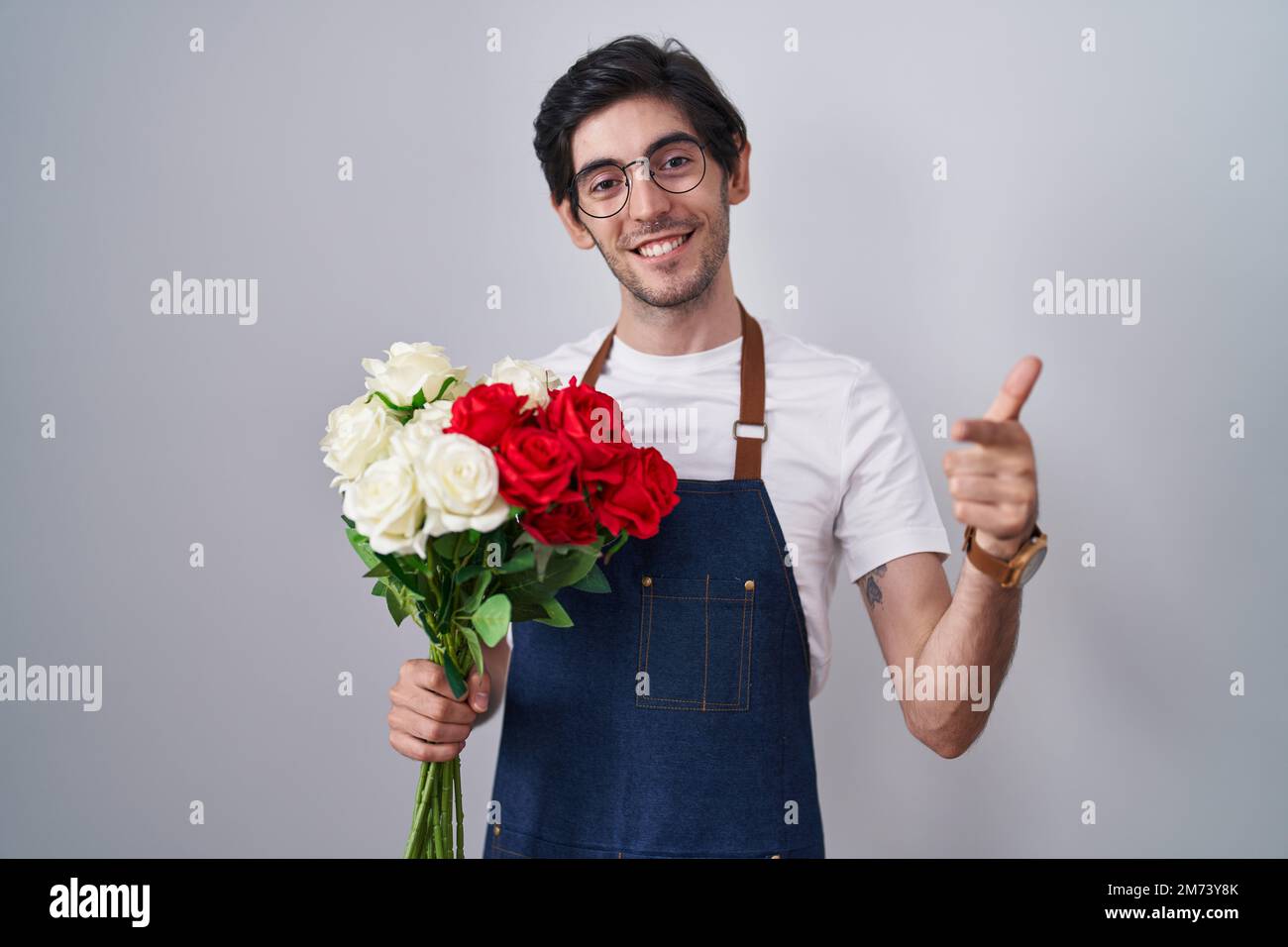 Young hispanic man holding bouquet of white and red roses pointing ...
