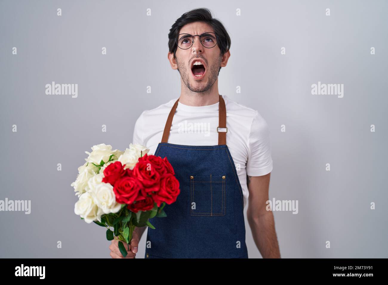 Young hispanic man holding bouquet of white and red roses angry and mad ...