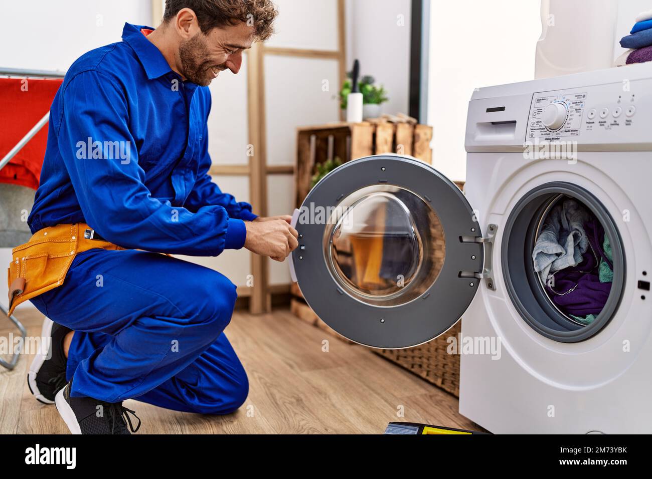Young hispanic man wearing handyman uniform repairing washing machine ...